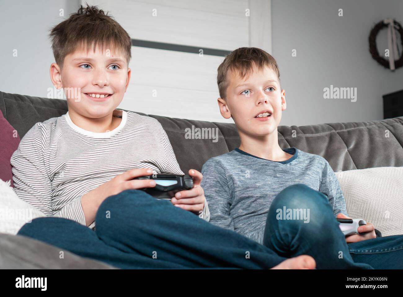 Happy school aged boys sit on sofa with game joysticks. Children play ...