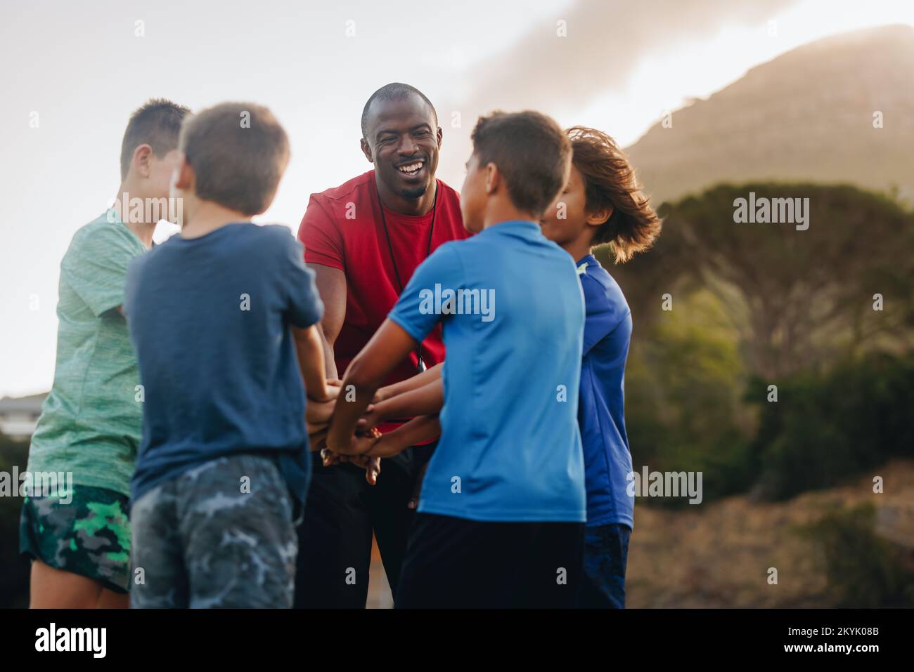 Rugby coach and his students putting their hands together in a huddle ...
