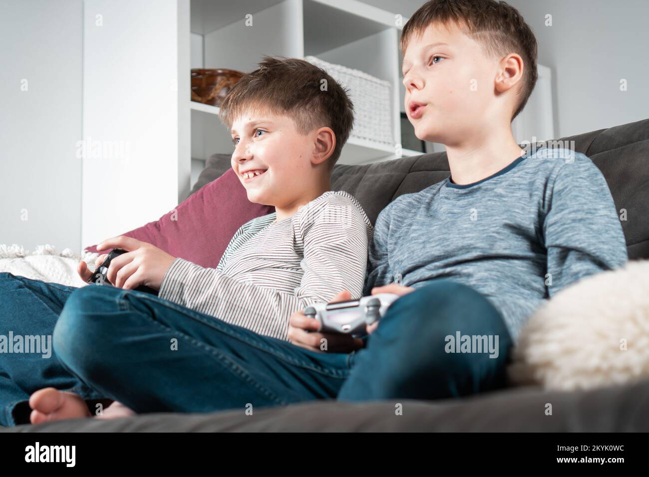 School aged boys sit on sofa with game joysticks, from below view ...