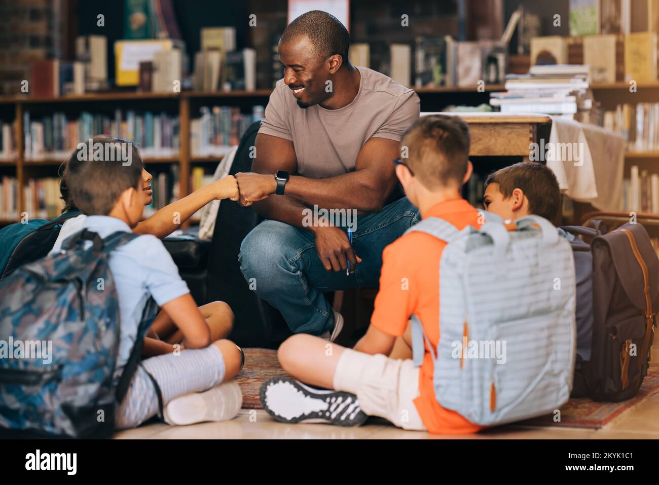 school teacher giving a student a fist bump in a library. Man teaching ...