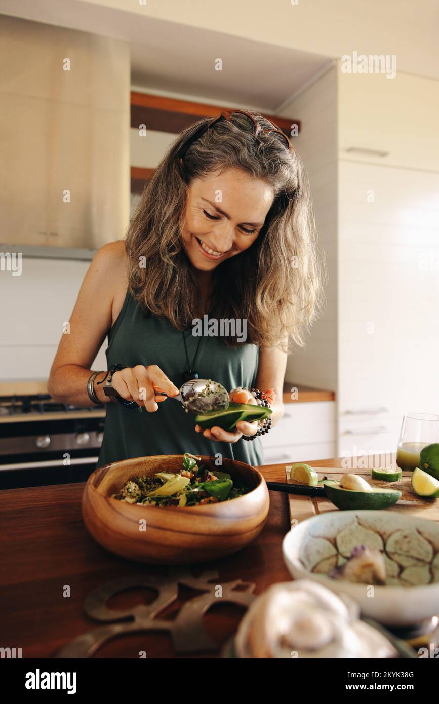 Happy vegetarian woman smiling while adding avocado to her buddha bowl ...