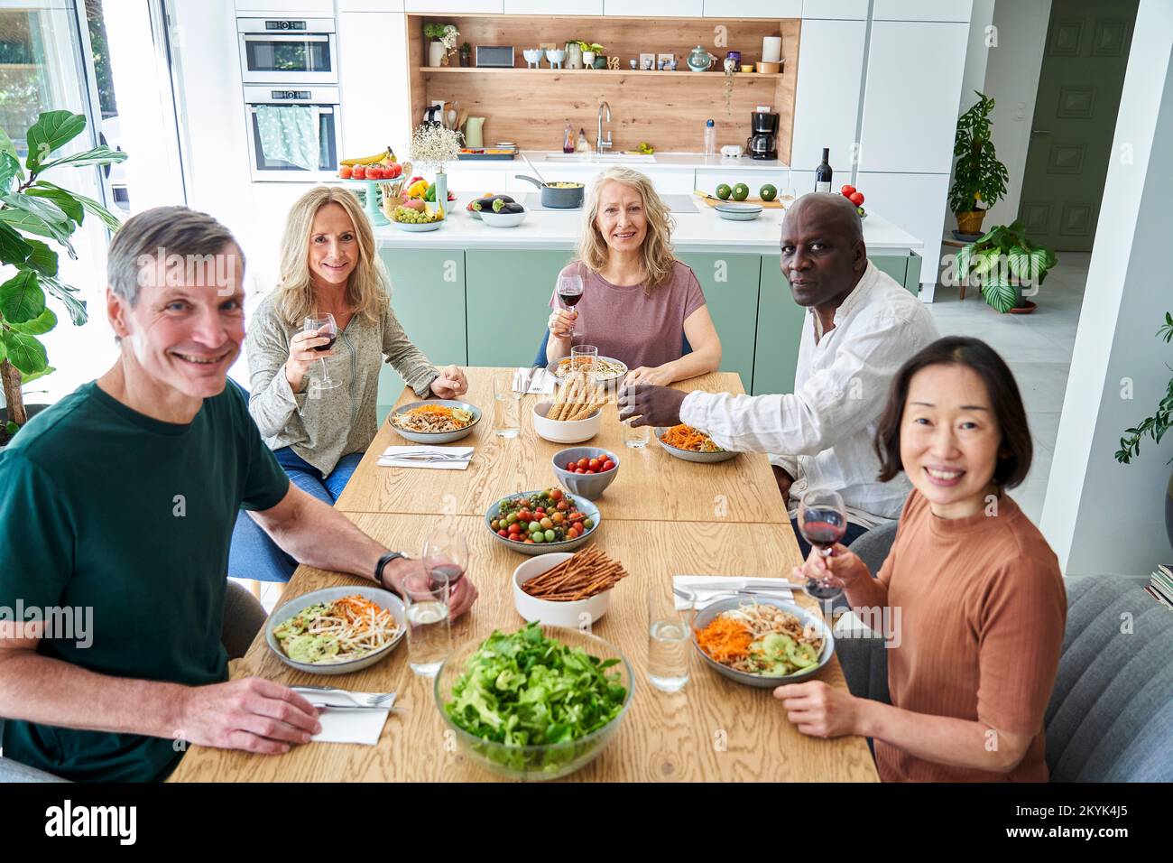 Group of fun mature diverse friends gathered at the table and raising ...