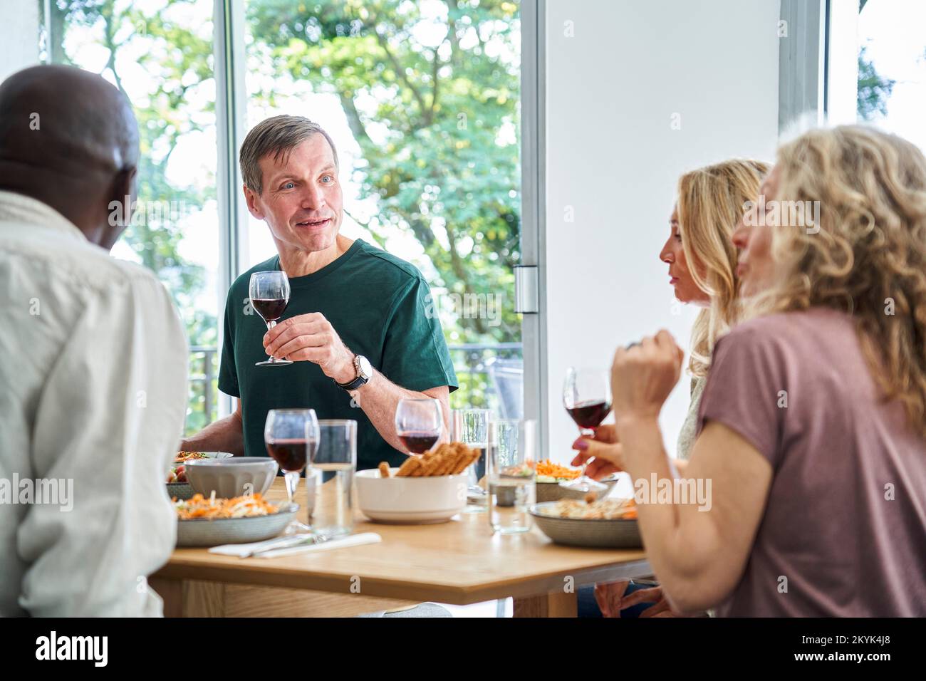 Group of fun mature diverse friends gathered at the table and raising ...