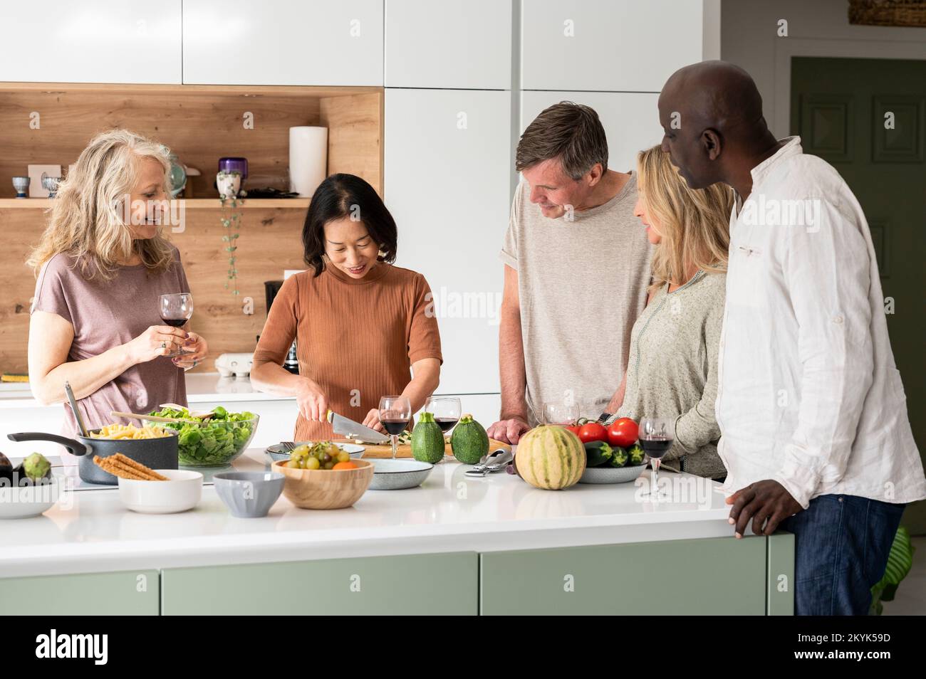 Group of diverse middle-aged friends chatting at kitchen island while ...