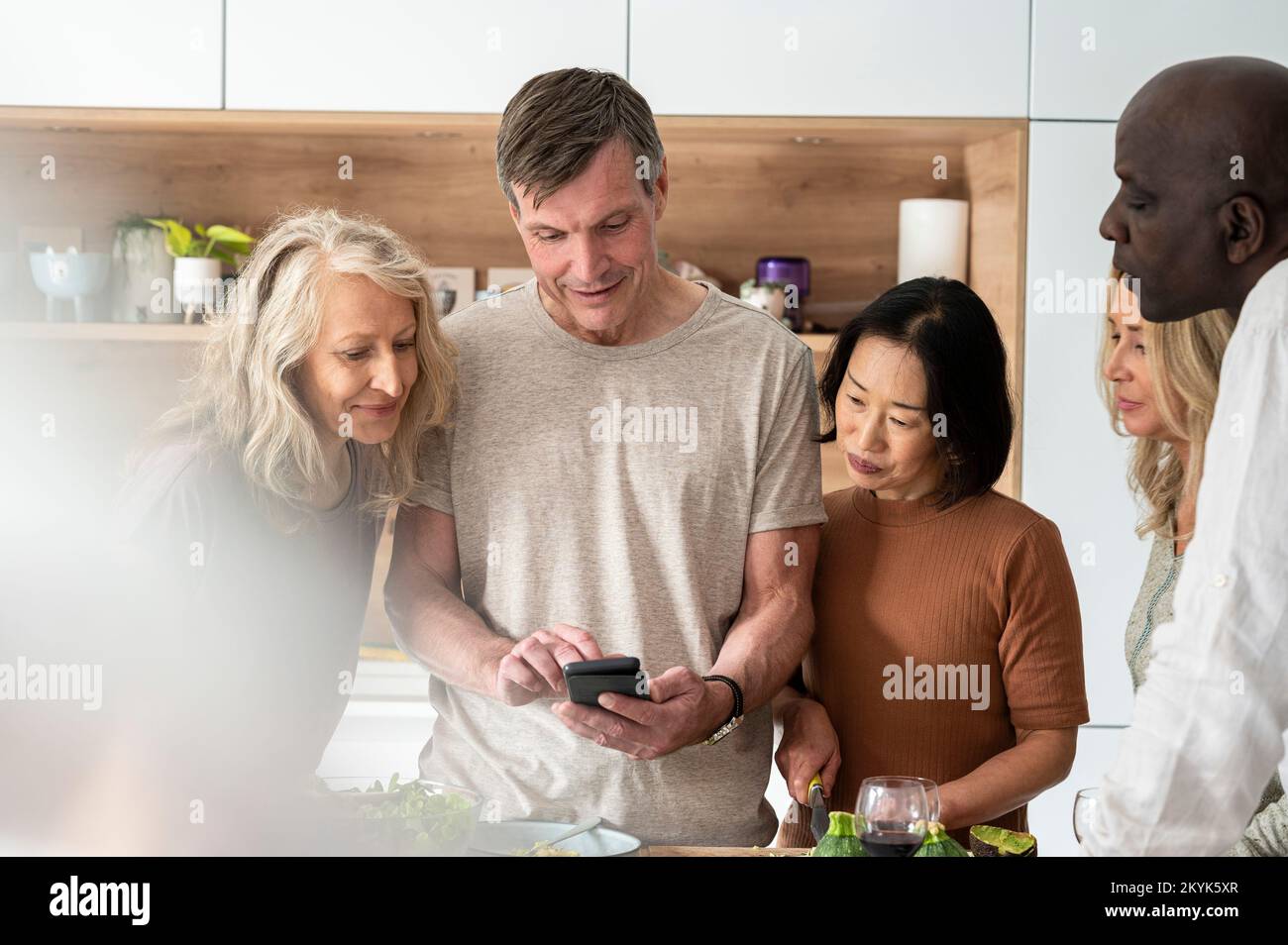 Diverse group of senior friends stading in the kitchen while checking ...