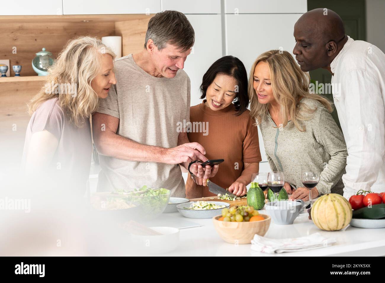 Diverse group of middle-aged friends checking a recipe while cooking ...
