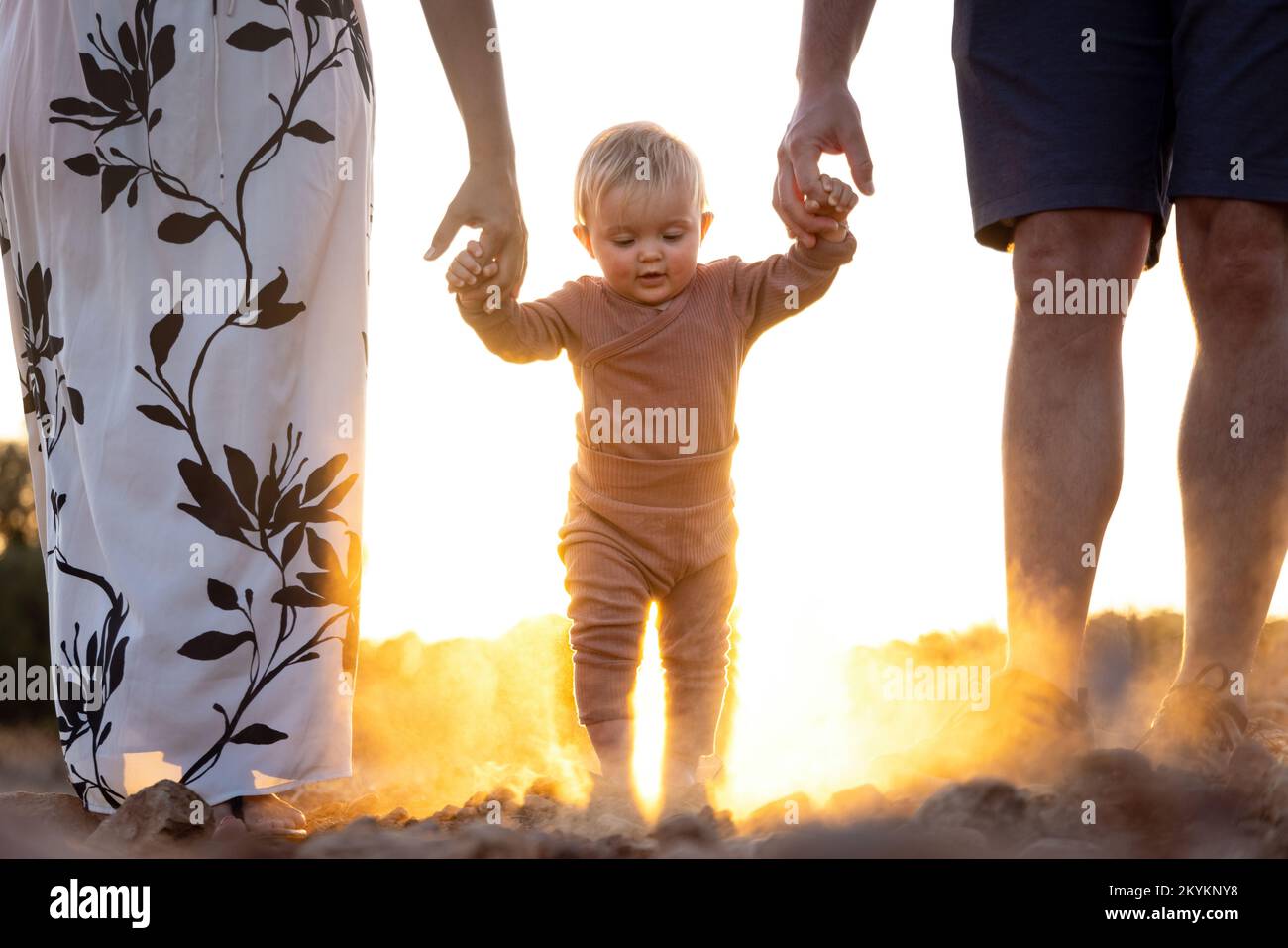 Little girl holding hands with her parents while learning how to walk ...