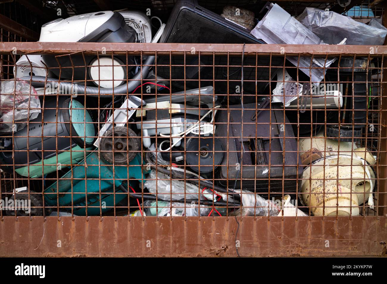 pile of mixed dirty electronic waste appliances in a metal cage at an ...