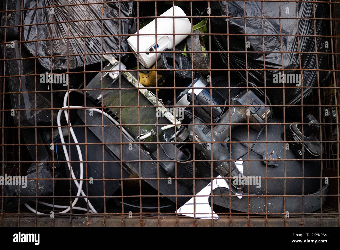 pile of mixed dirty electronic waste appliances in a metal cage at an ...