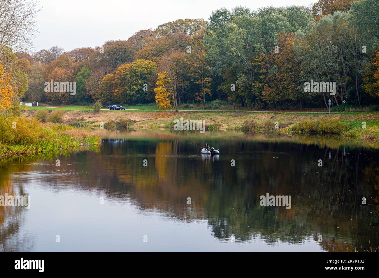 fisherman in a rubber boat on the river and colorful autumn trees on ...