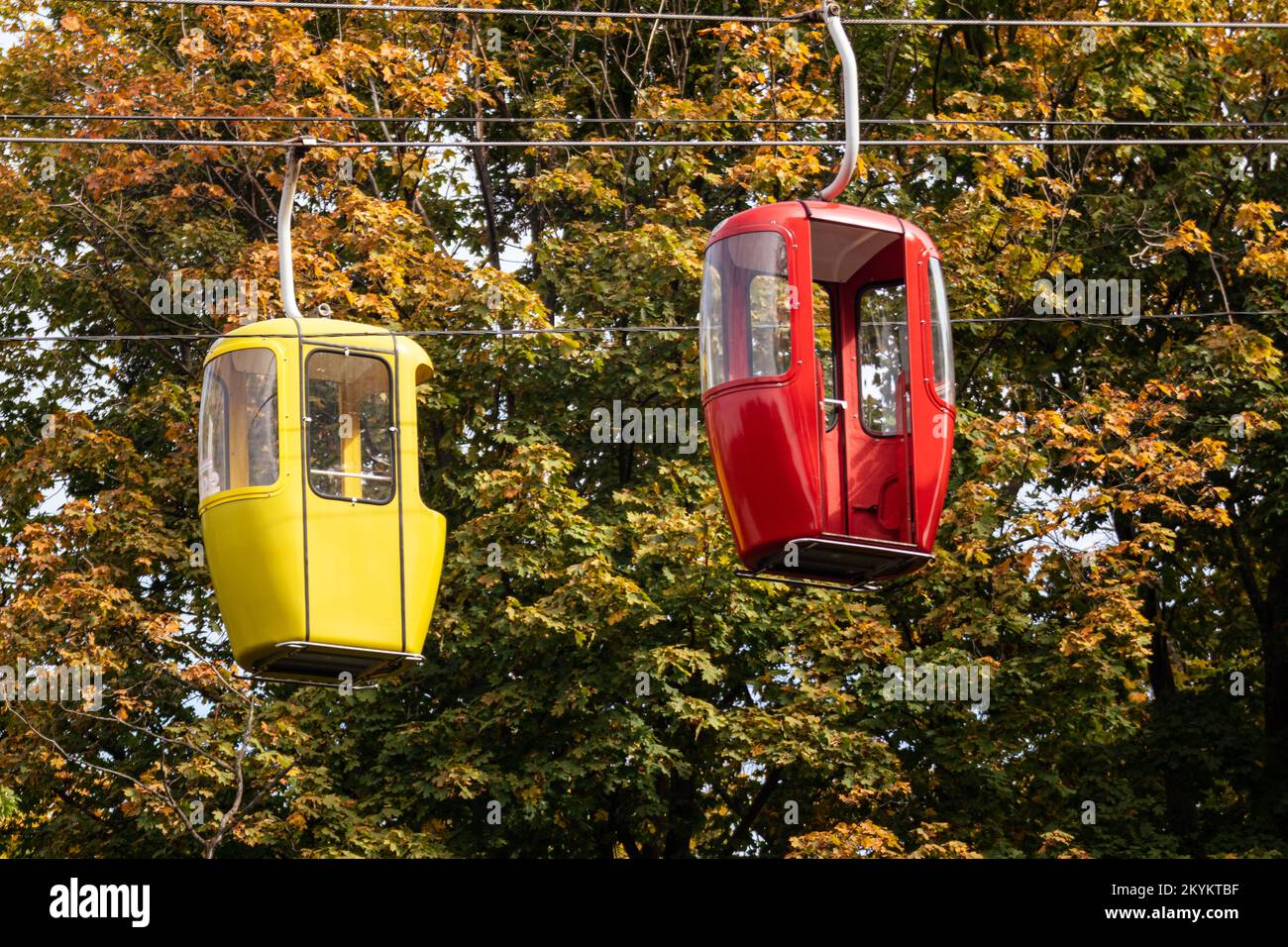 Colored red and yellow cableway cabins in autumn trees. Funicular ...