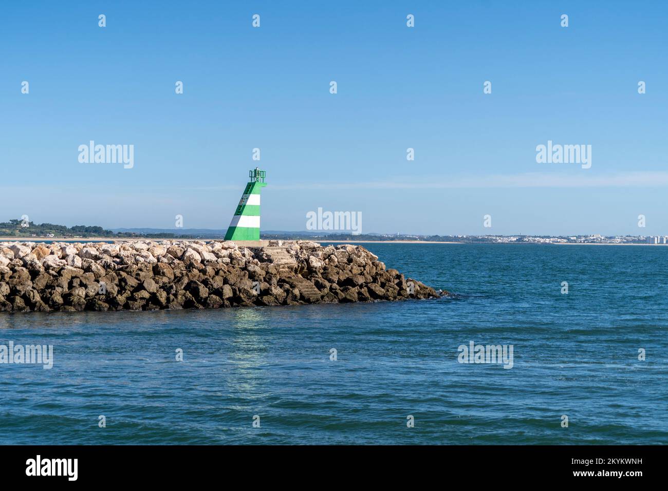 Lighthouse on a rock pier painted in green and white. Blue ocean and ...