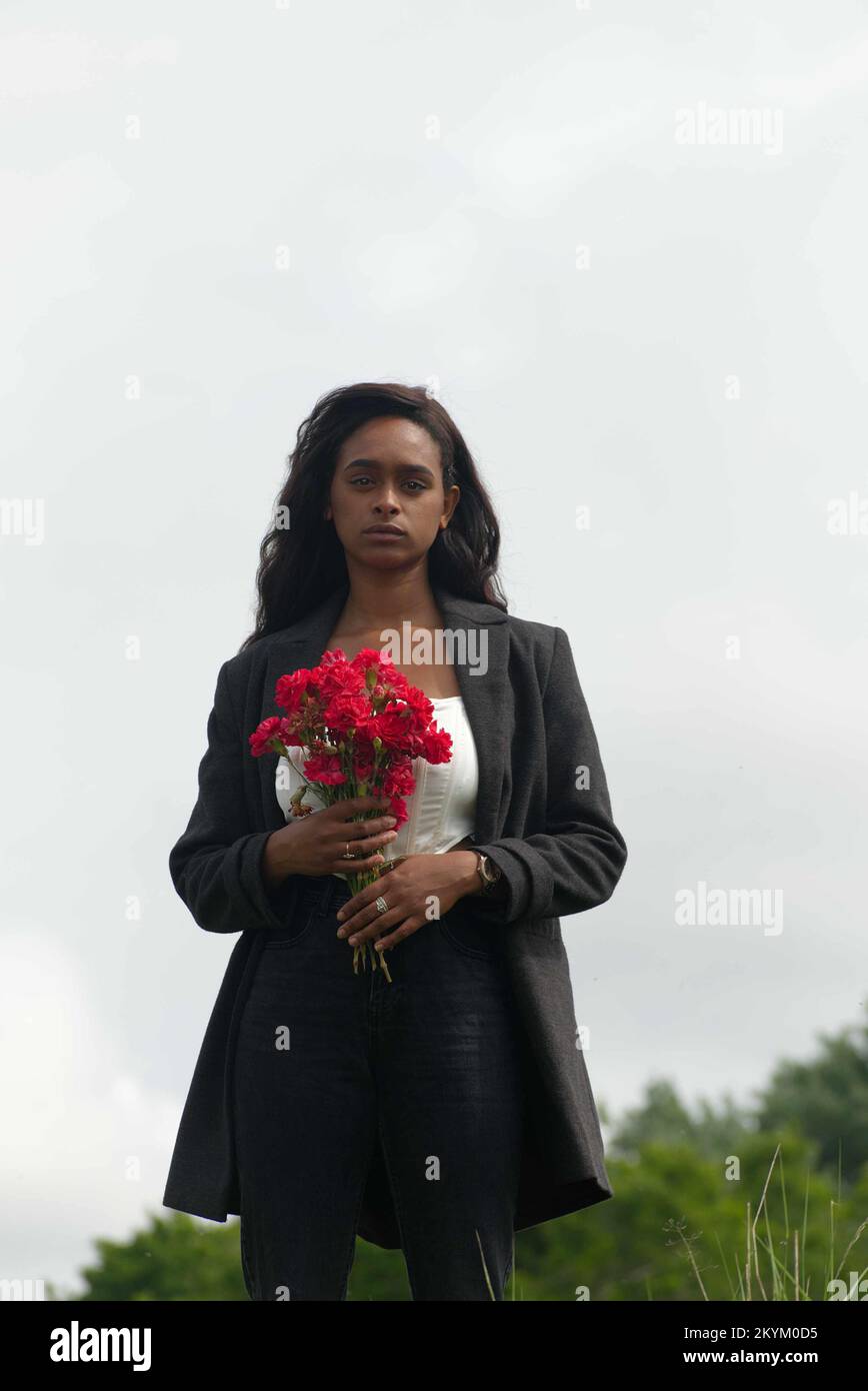 young black woman holding a bunch of red flowers looking melancholy ...
