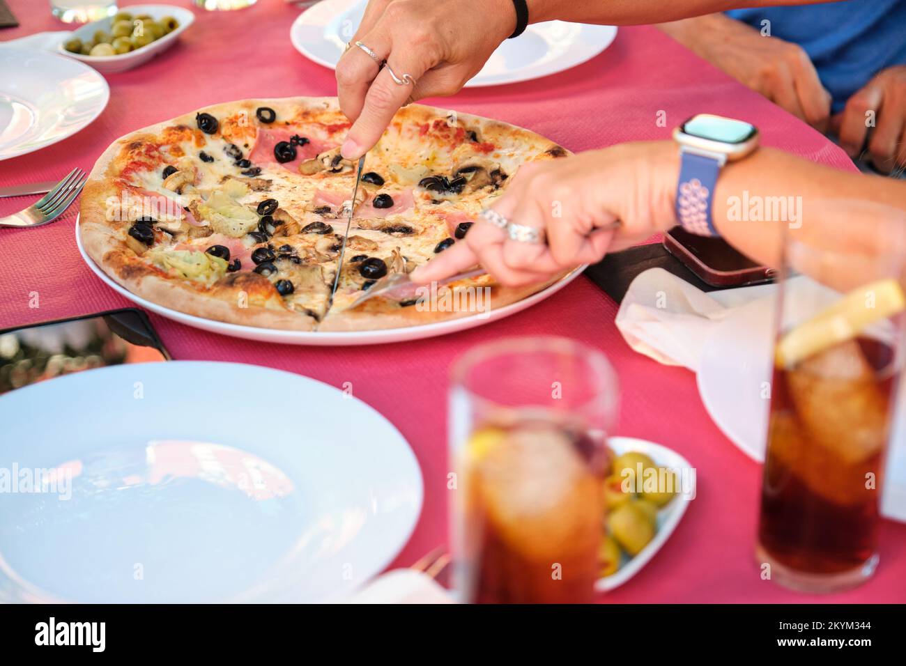 Hands cutting pizza to share in a restaurant table Stock Photo - Alamy