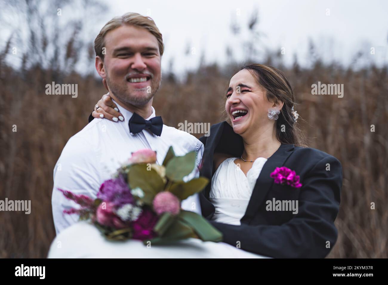 Young groom holding his joyful bride in a white dress in his arms ...