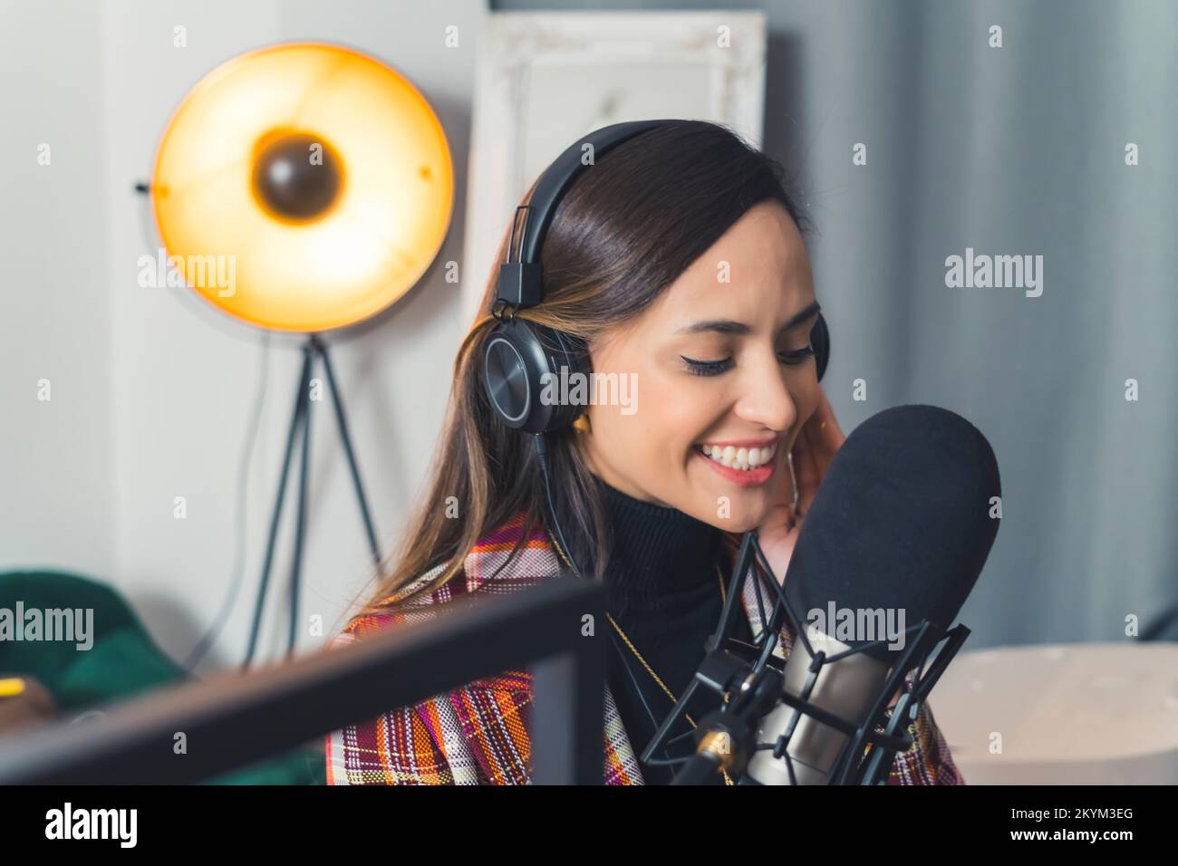 Young smiling brunette woman with microphone recording at home studio ...