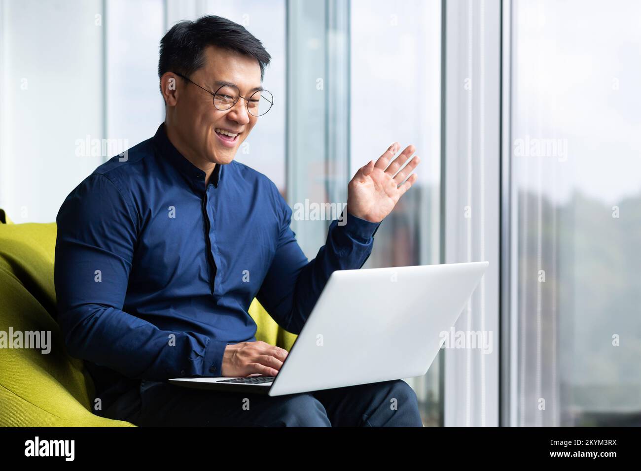 Video call, successful asian businessman near window in office talking remotely, online meeting ...