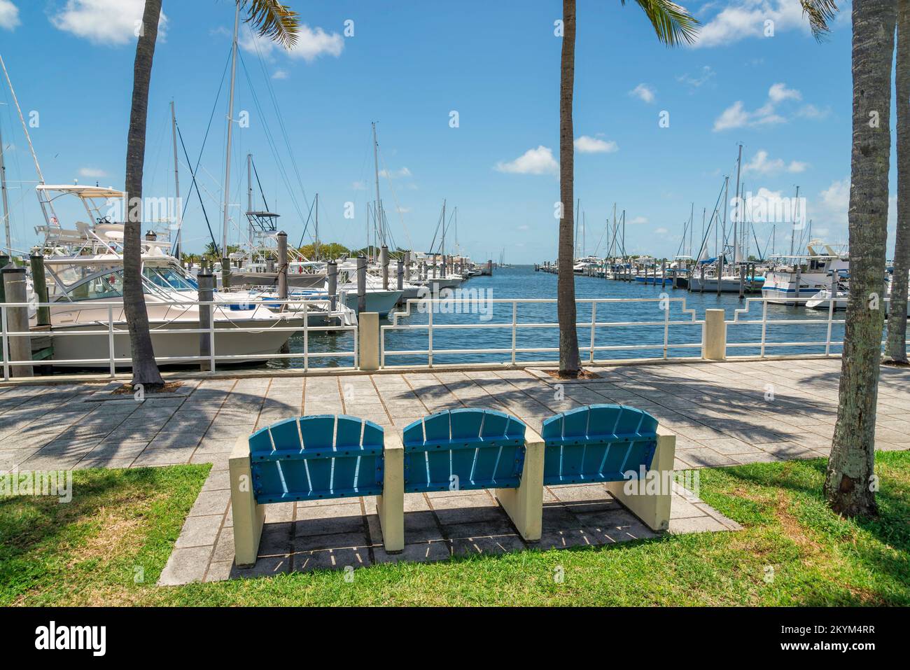 Bench on a sidewalk pathway facing the views of the boats at the marina ...