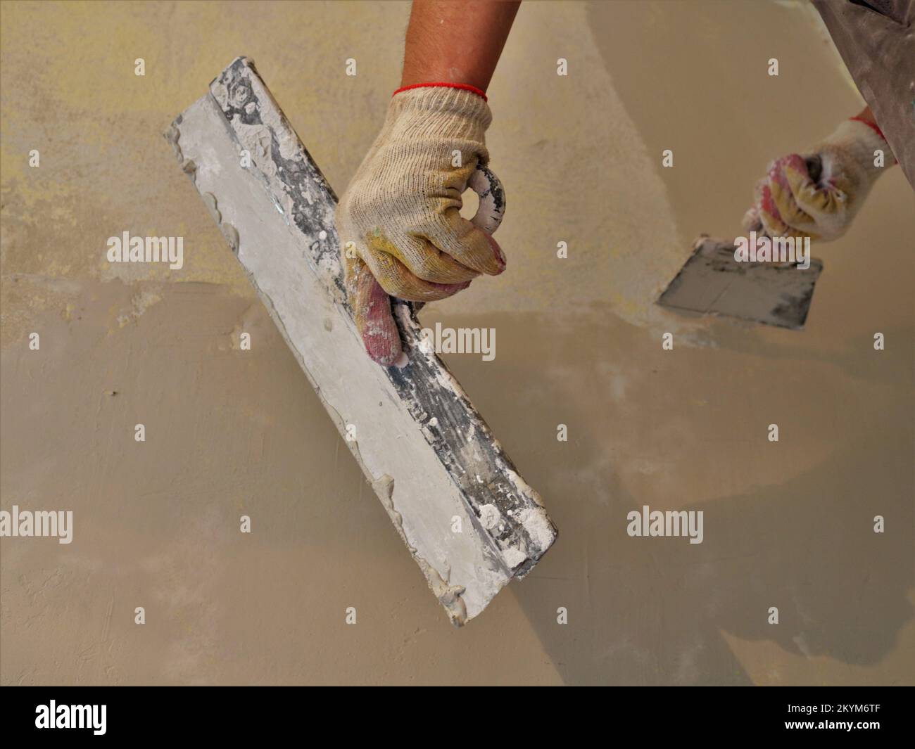 hands of a plasterer with two spatulas at work near the wall ...