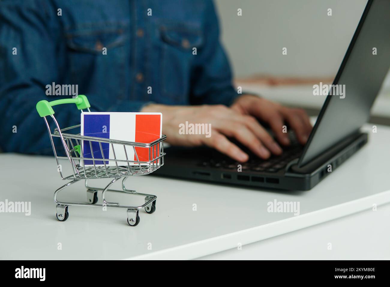 Small shopping cart with flag of France on the table. Man using laptop ...