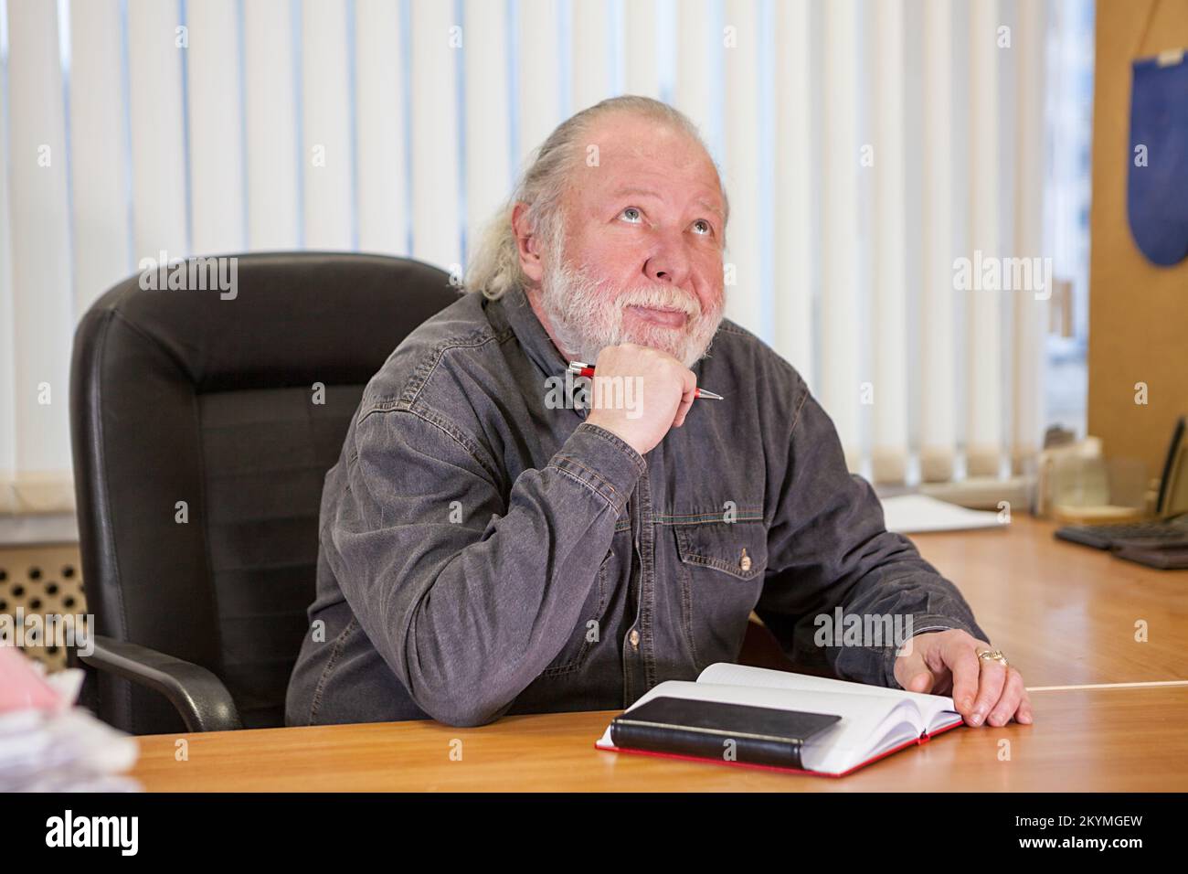 A senior man looks up thoughtfully, a pensioner at the workplace in a ...