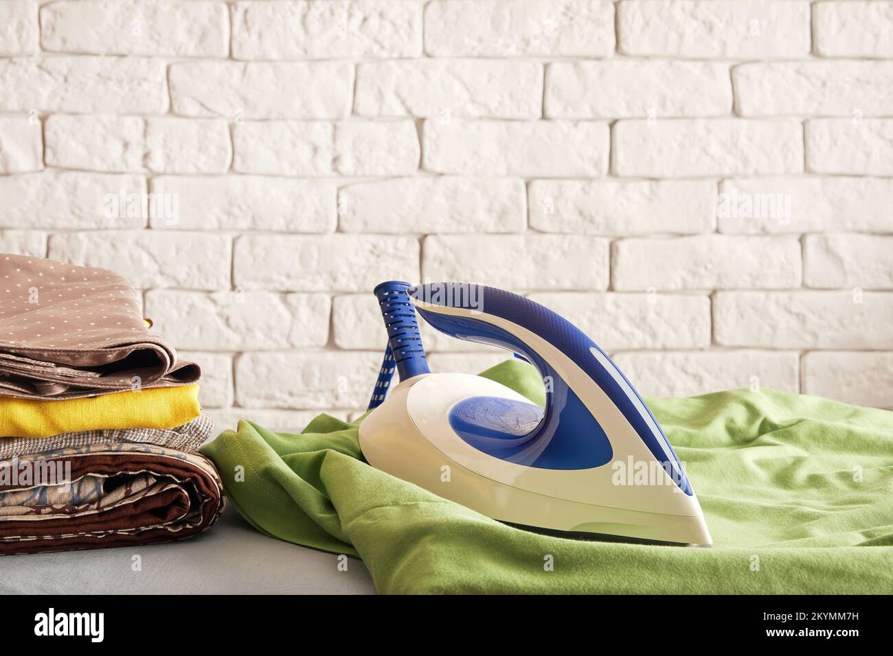 Stack of colour clothes and iron smooths green shirt on the board ...