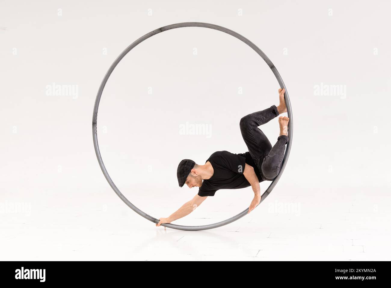 Barefoot male in black outfit and cap doing trick in metal Cyr wheel on ...