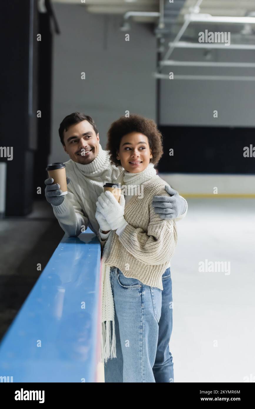 Smiling man hugging african american girlfriend with coffee to go on ...
