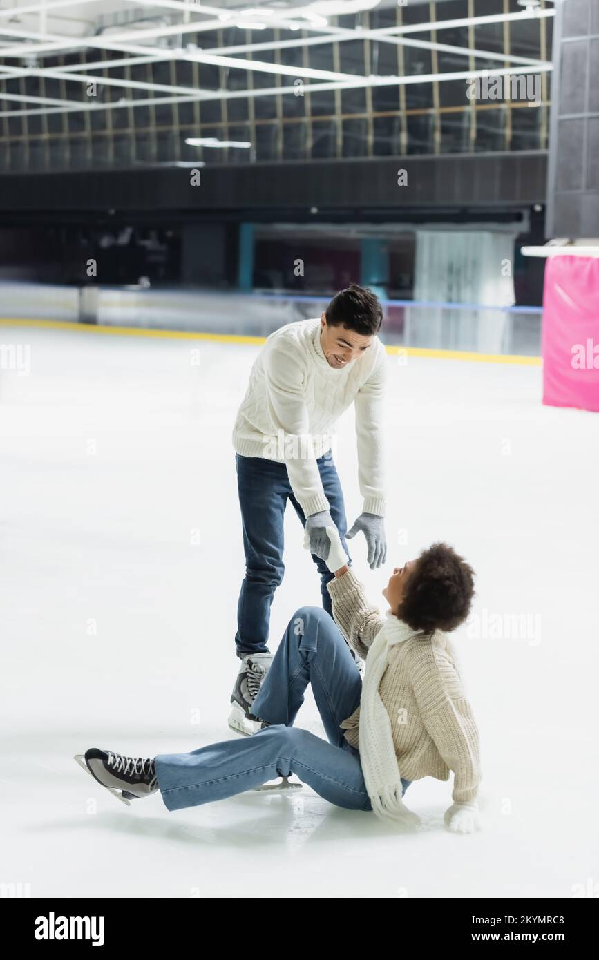 Young man giving hand to african american girlfriend falling on ice ...
