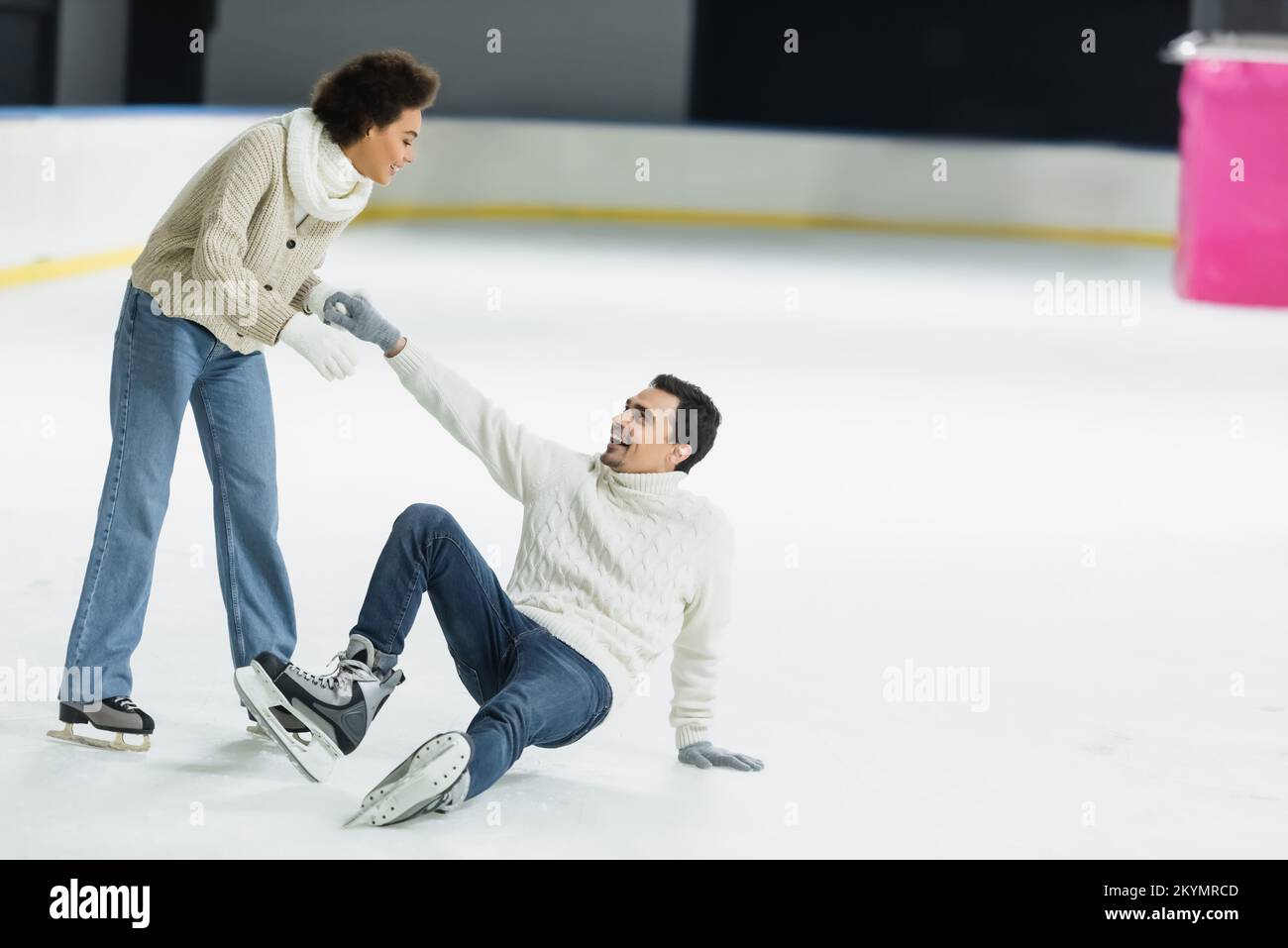 Smiling african american woman helping boyfriend falling on ice rink ...