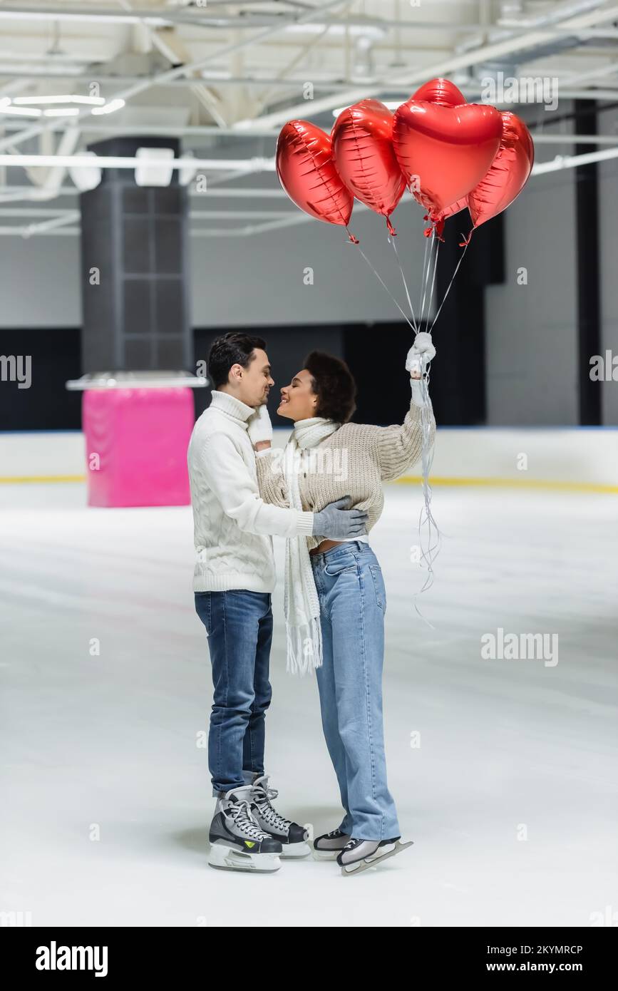 Side view of cheerful african american woman holding balloons in heart ...