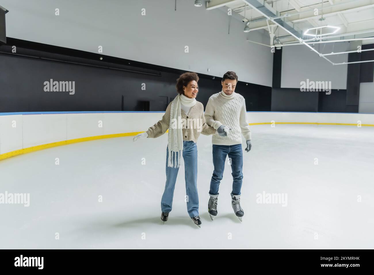 Young interracial couple holding hands while ice skating on rink Stock ...