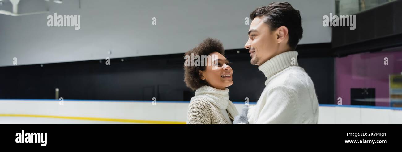 Positive african american woman in scarf looking at boyfriend on ice ...