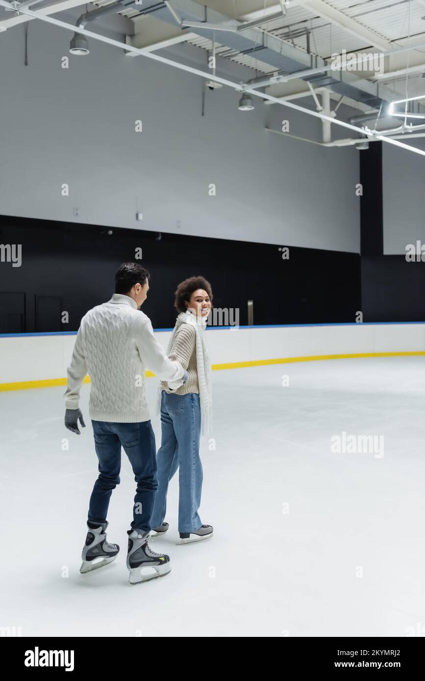 Cheerful african american woman holding hand of boyfriend while ice ...