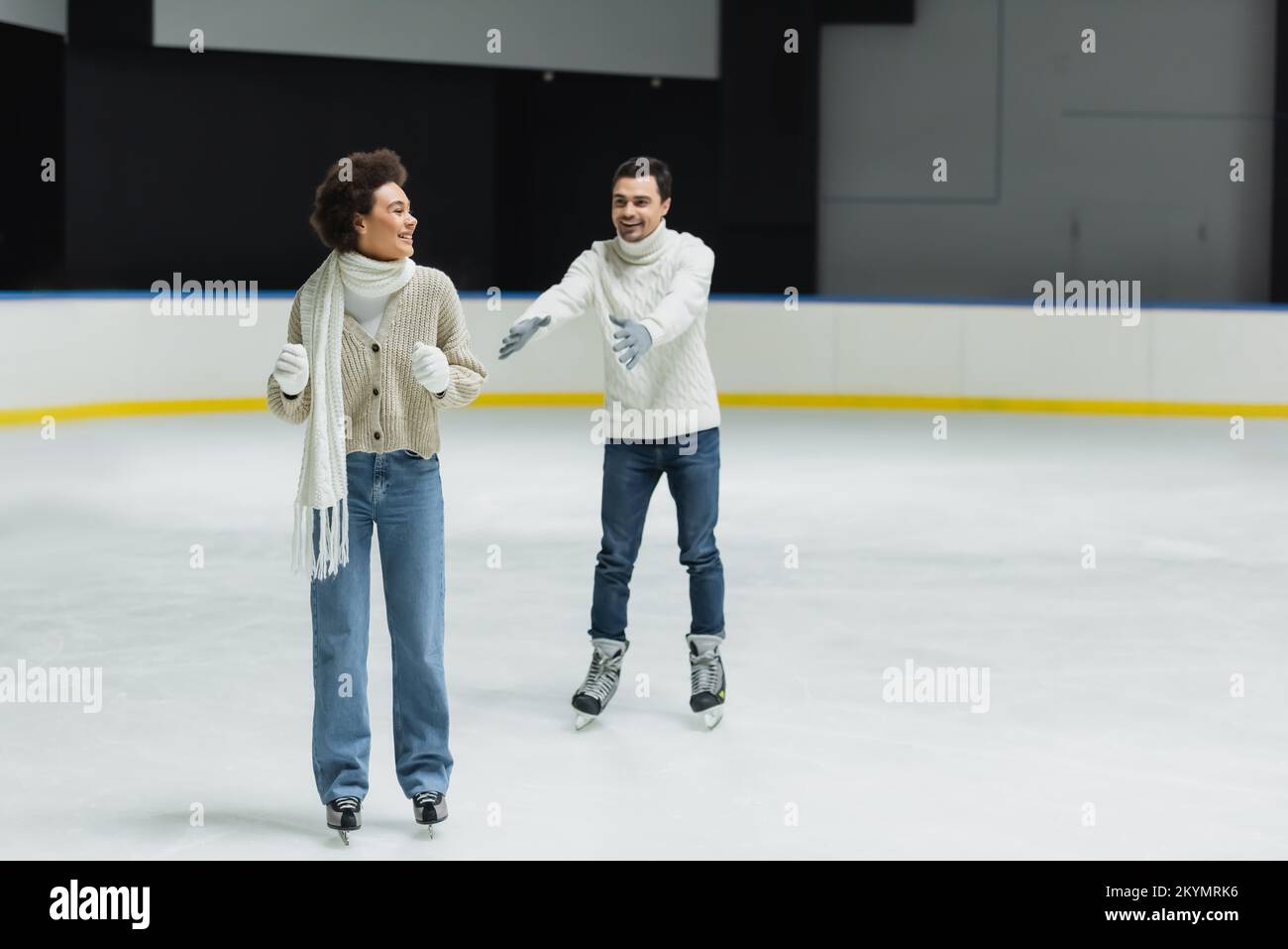 Smiling man outstretching hands to african american girlfriend ice ...