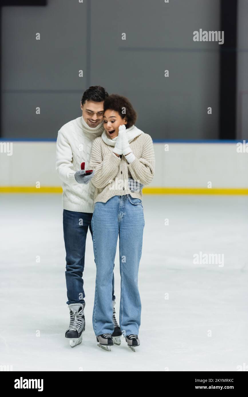Smiling man holding engagement ring near excited african american ...