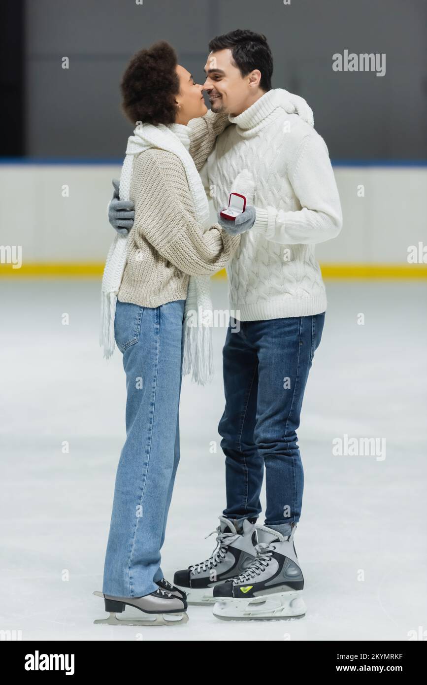 Side view of multiethnic couple with proposal ring kissing on ice rink ...