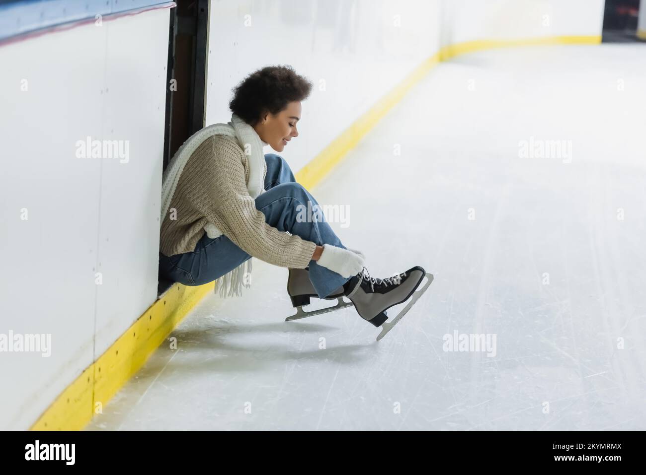 Side view of smiling african american woman wearing ice skates on rink ...
