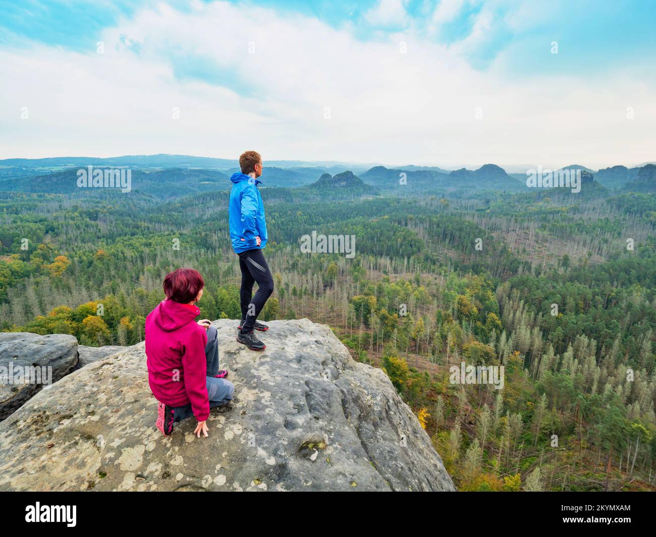 Boy and girl tourists stay on cliff and thinking. Forest in valley with ...