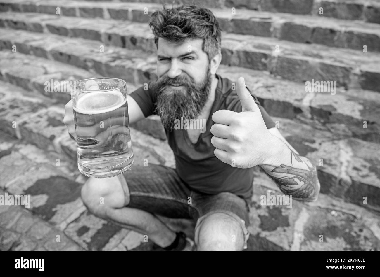 Man with beard and mustache holds glass with beer and shows thumb up ...