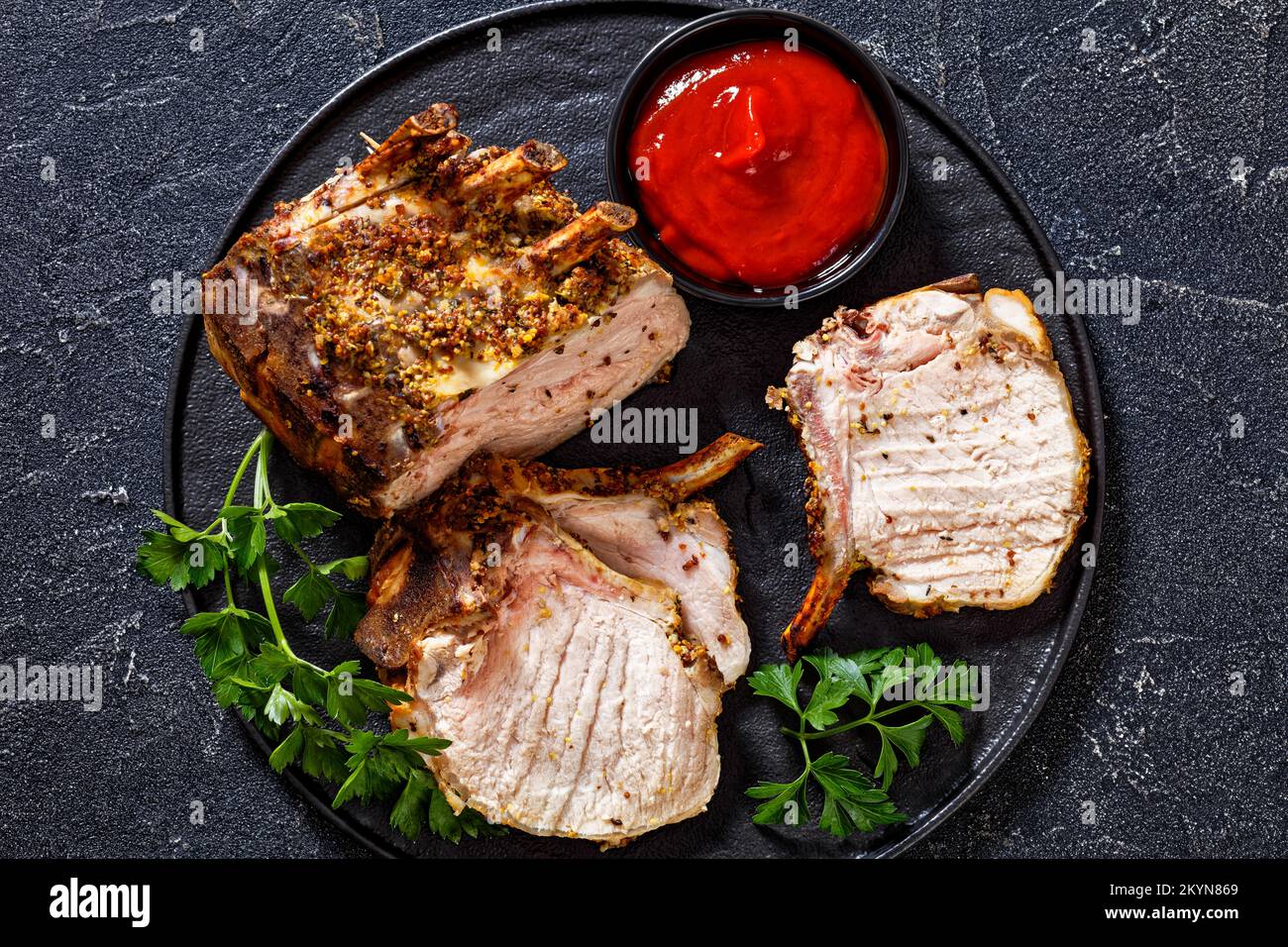 Standing Pork Rib Roast cut on chops on black plate with tomato sauce ...