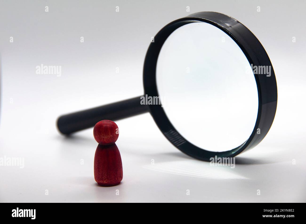 Red wooden figure looking through a magnifying glass with white ...