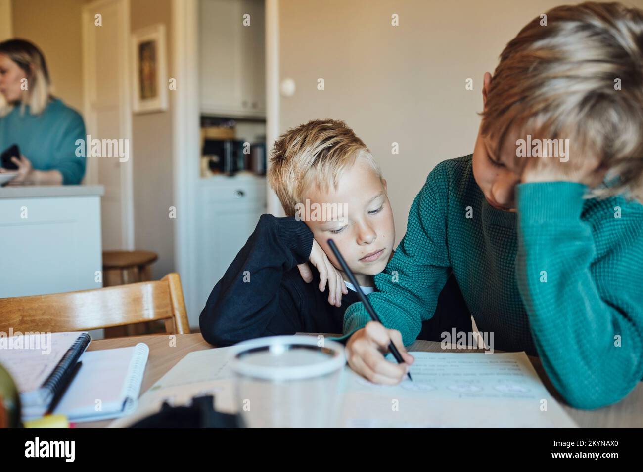 Boy leaning on elbow while looking at brother doing homework Stock ...
