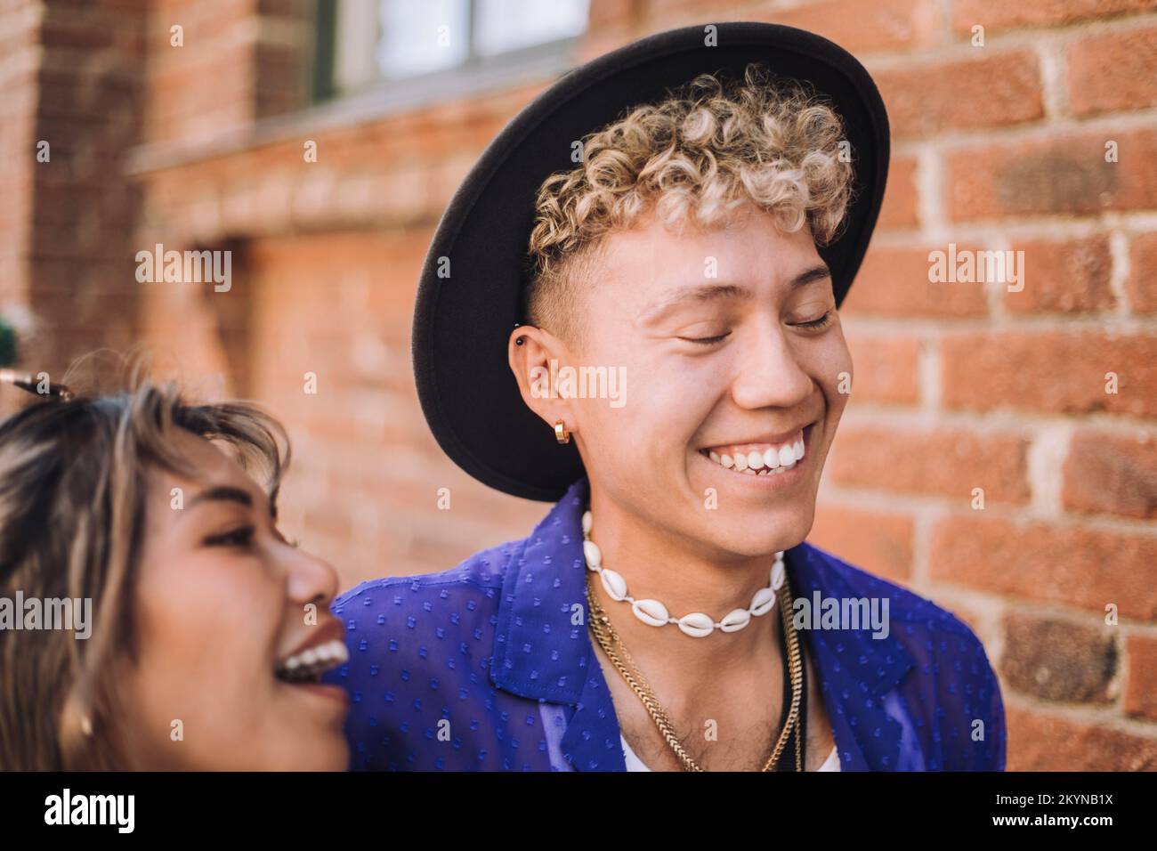 Happy young man wearing hat by female friend laughing against building ...