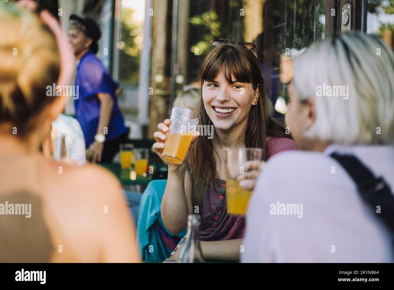 Happy transgender woman talking while enjoying juice with non-binary ...