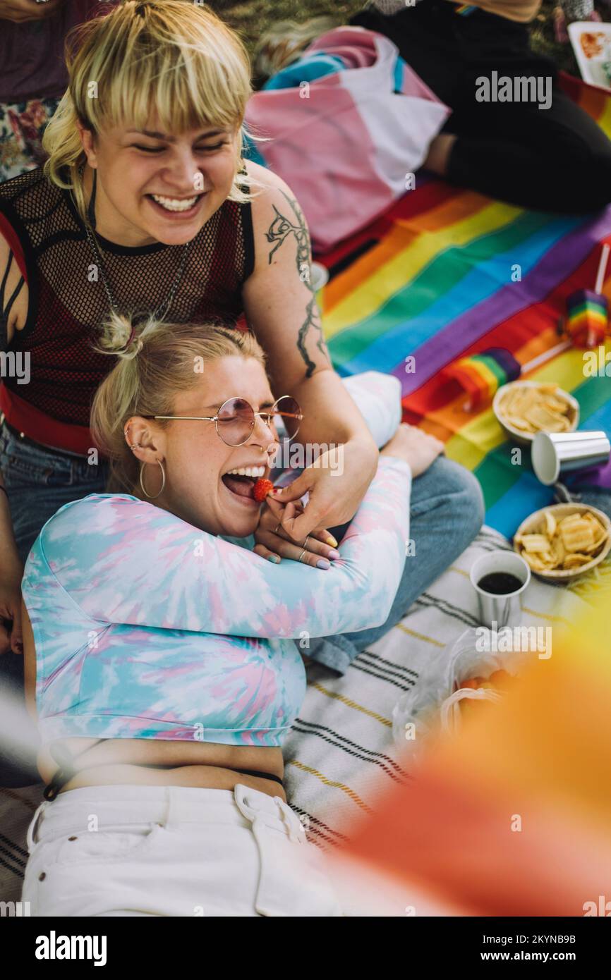 Happy non-binary person feeding strawberry to female friend lying on ... Happy non-binary person feeding strawberry to female friend lying on ...