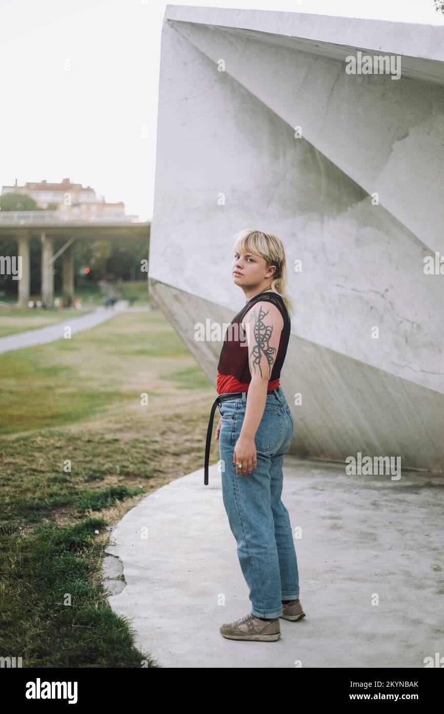 Side view of non-binary person standing near wall at park Stock Photo ...