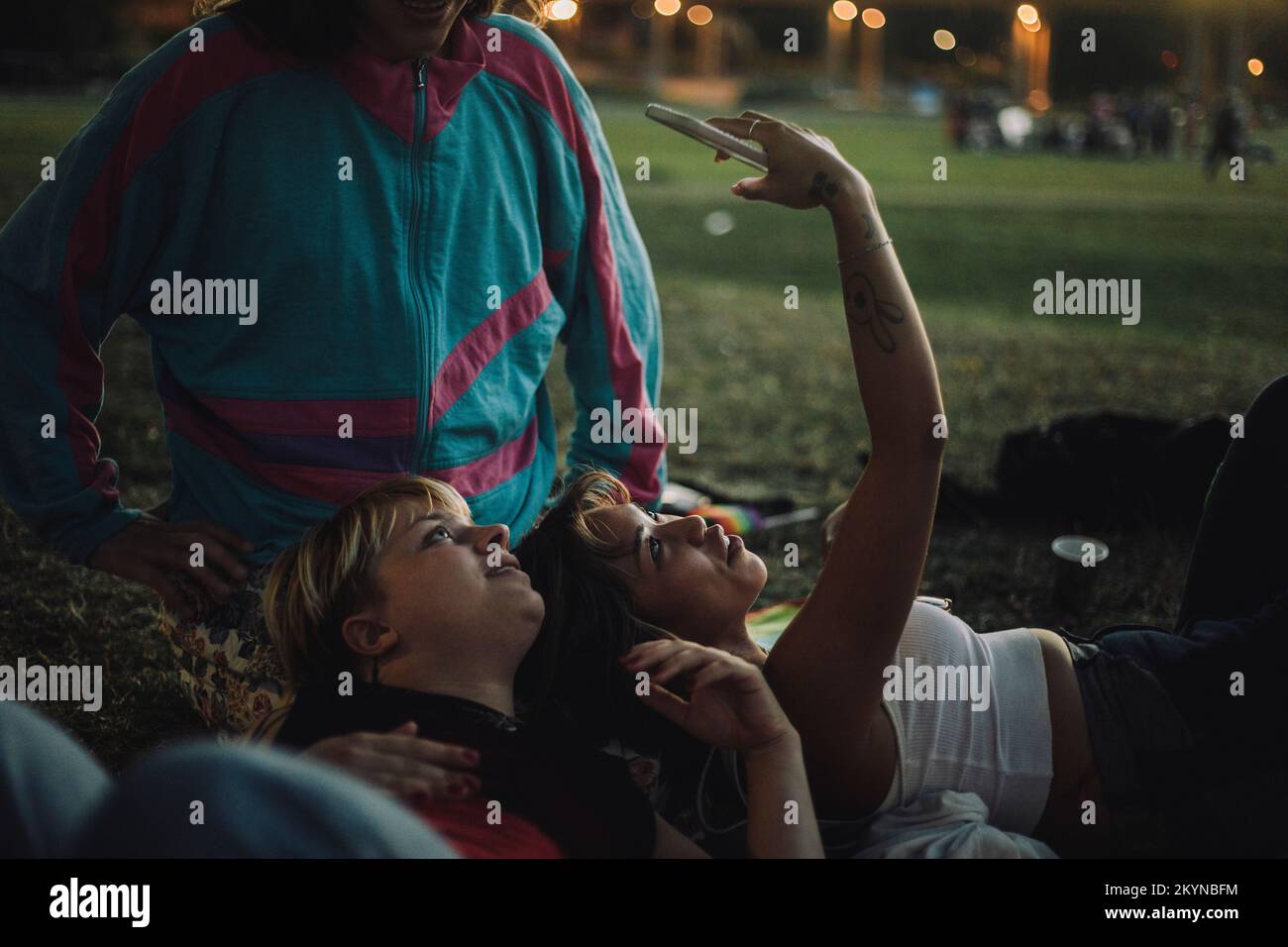 Young woman taking selfie with non-binary person while lying on friend ...