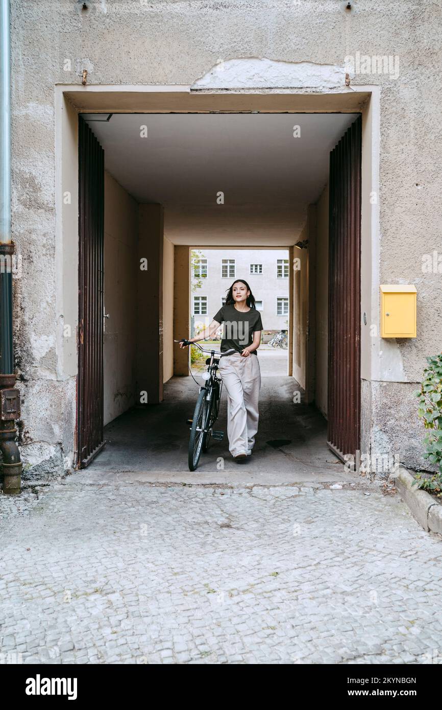 Woman wheeling with bicycle while walking out of archival doorway Stock ...