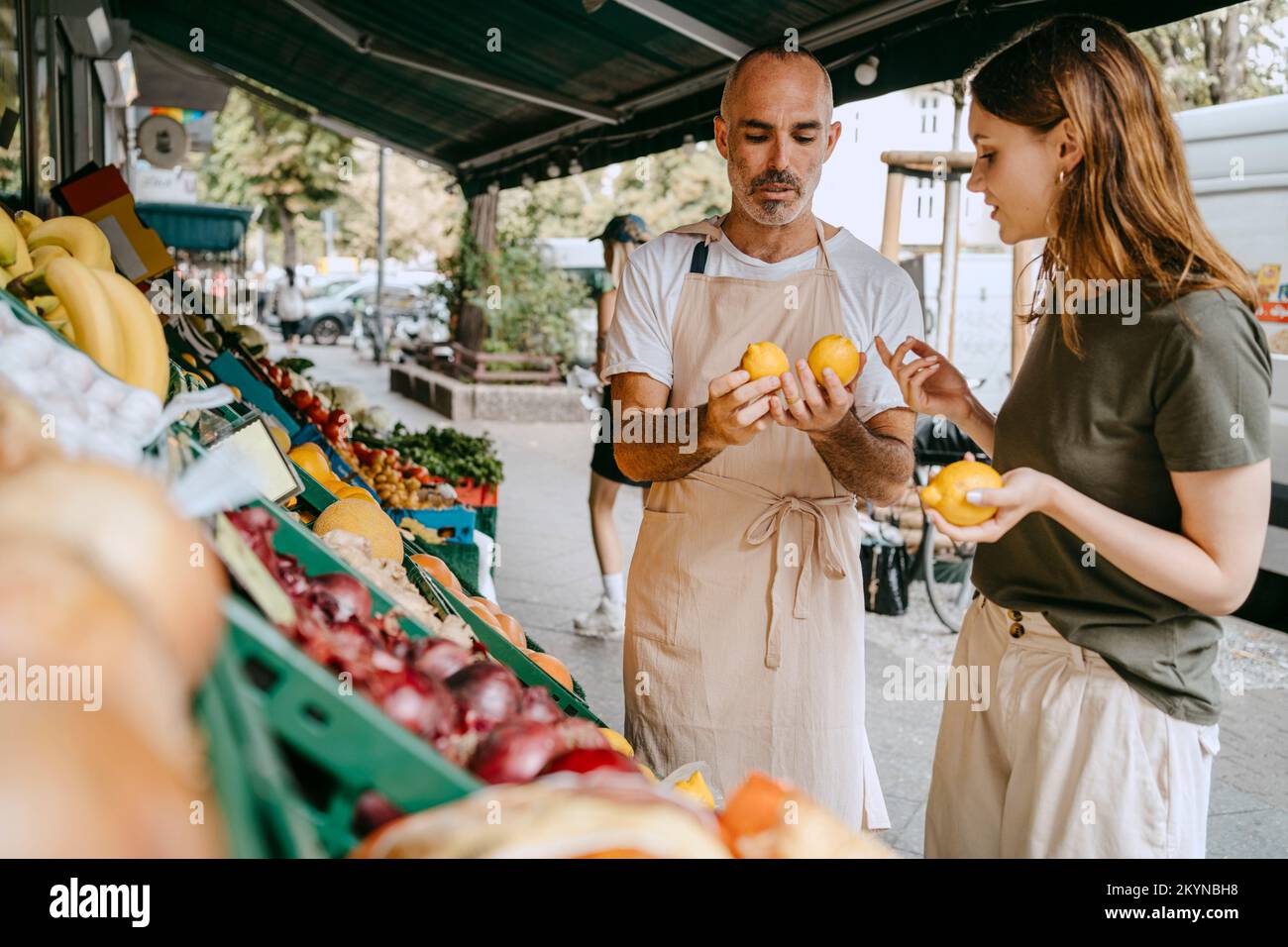 Male vendor wearing apron while assisting female customer buying lemons ...